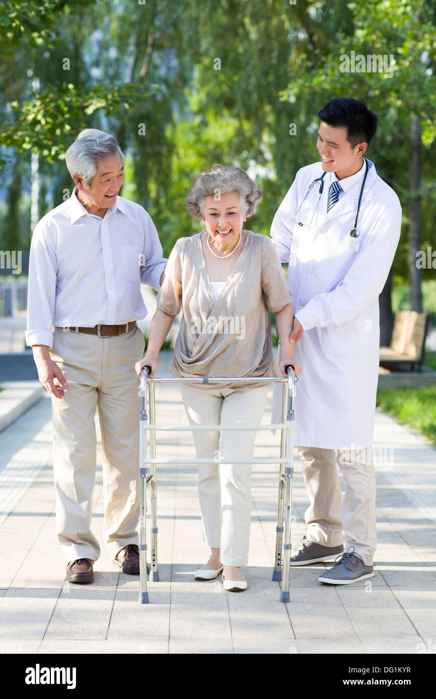 Senior woman walking with walking frame under doctor and husband's ...