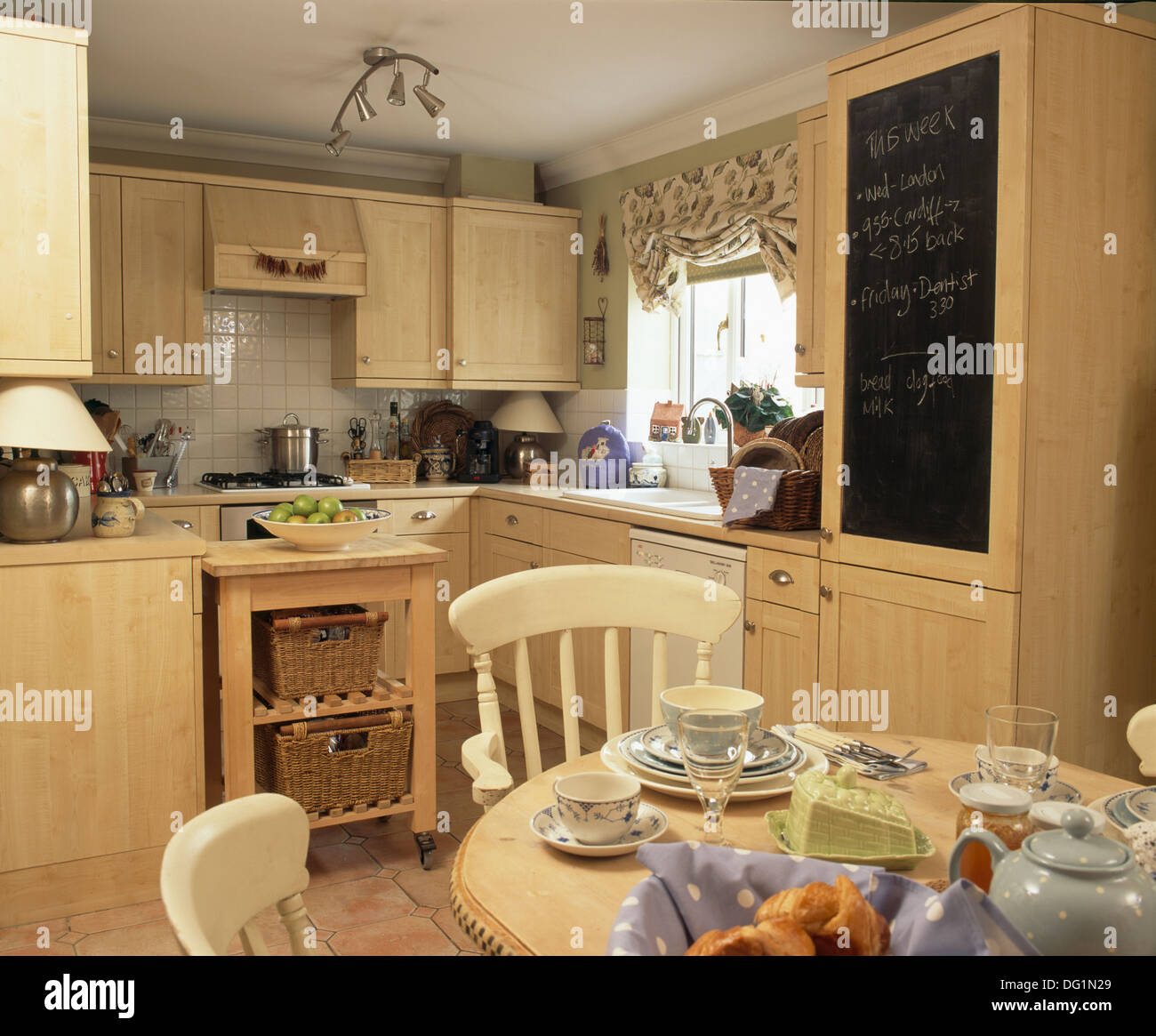 Circular table set for breakfast in neutral kitchen with blackboard on ...