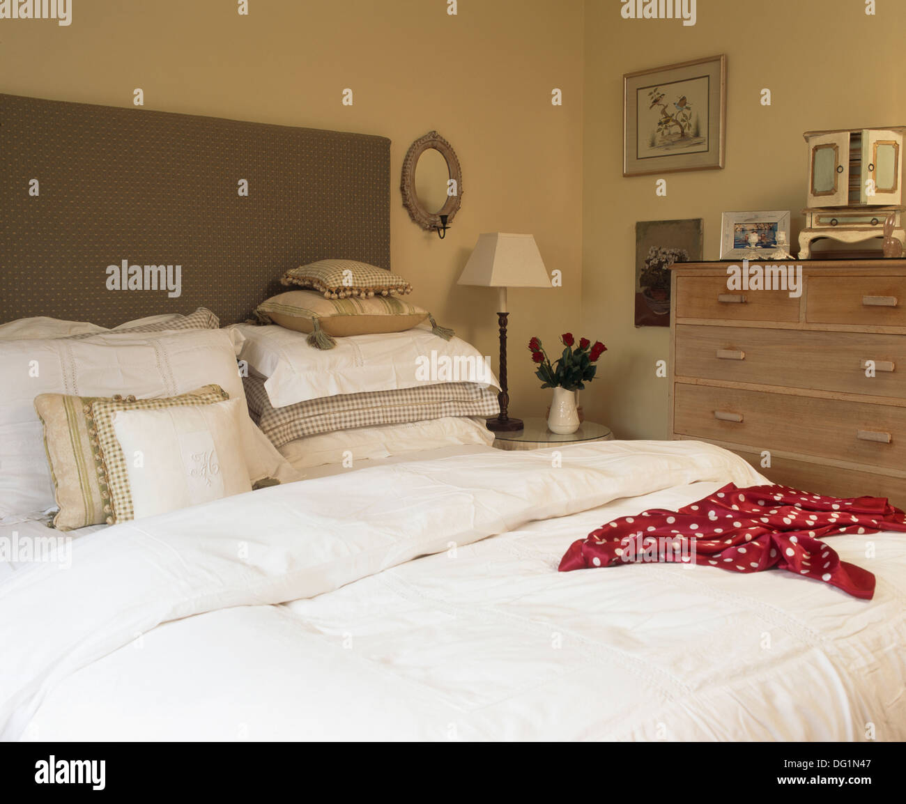Pillows and cushions piled on bed with brown upholstered headboard and ...