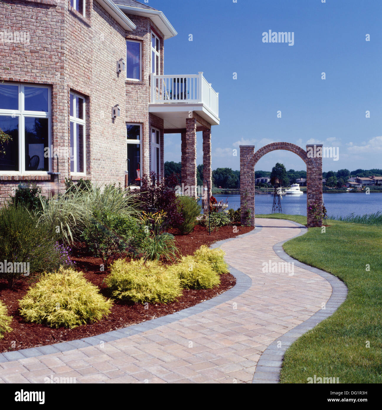 Curved, paved path between lawn and border with low shrubs and bark ...