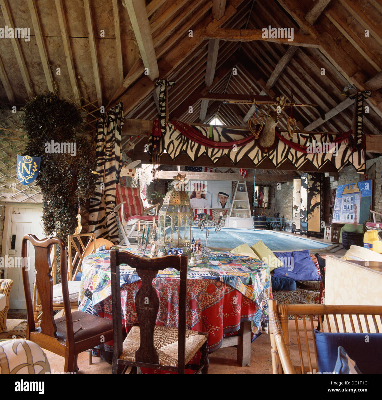 Chairs and table with patchwork cloths in foreground of cluttered barn ...