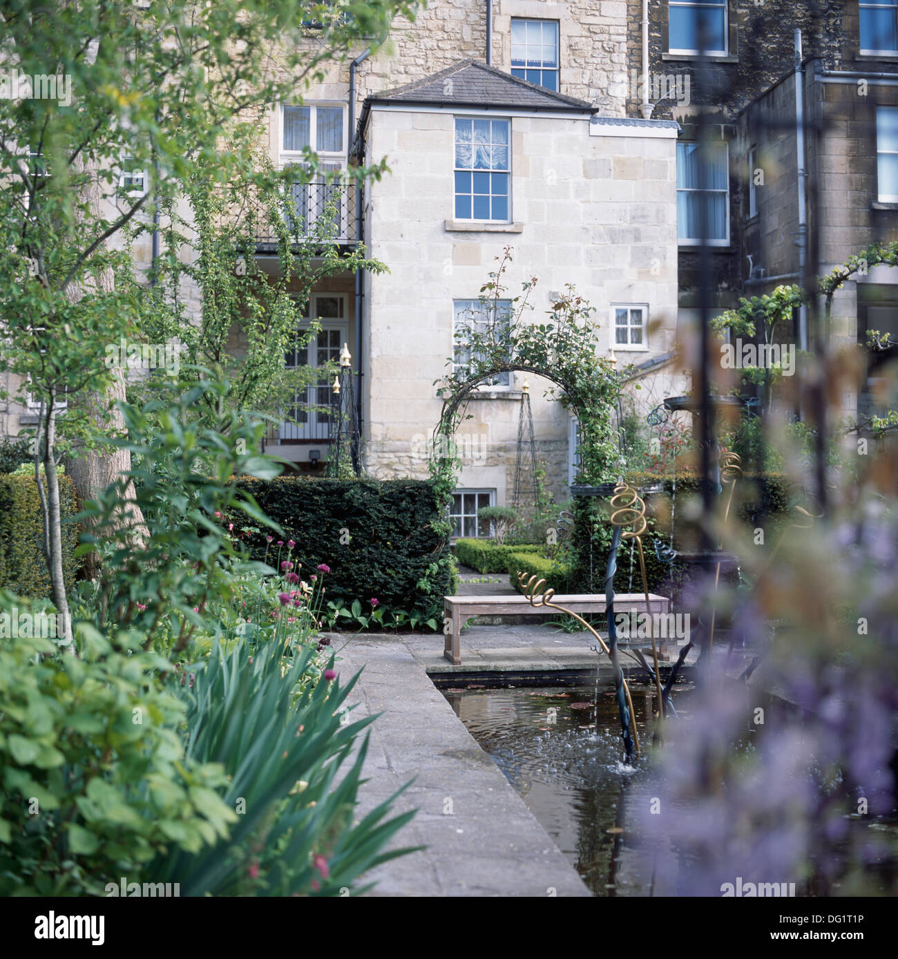 Rectangular pond with fountain in paved town garden with clipped hedge ...