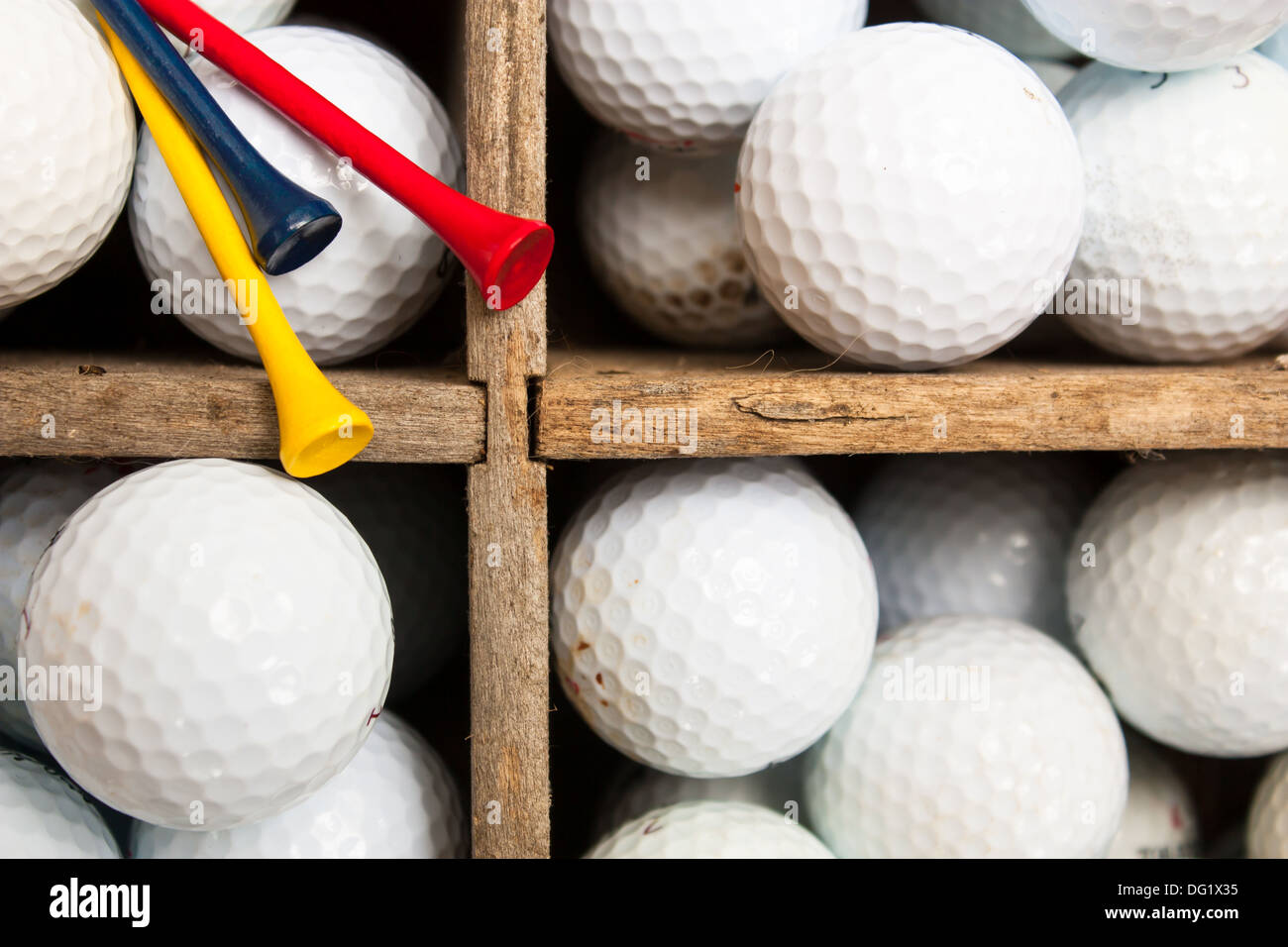 Used golf balls and colored wooden tees in a weathered antique wooden ...