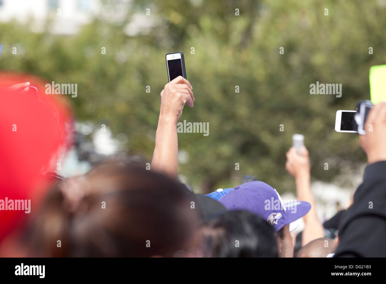 Man using an iPhone to video tape an outdoor event over crowd of people ...