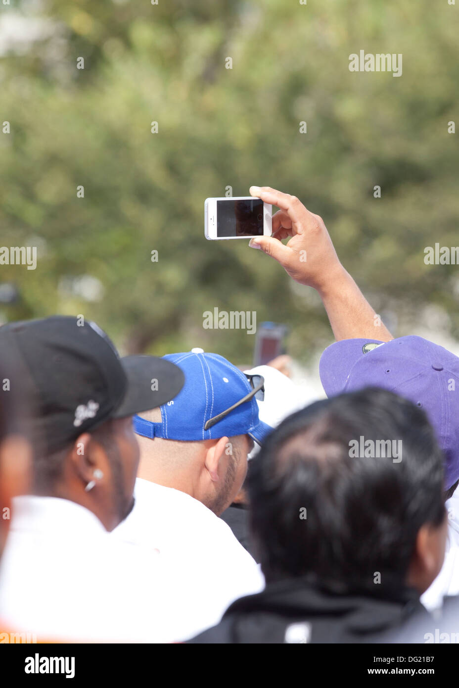 Man using an iPhone to video tape an outdoor event over crowd of people ...