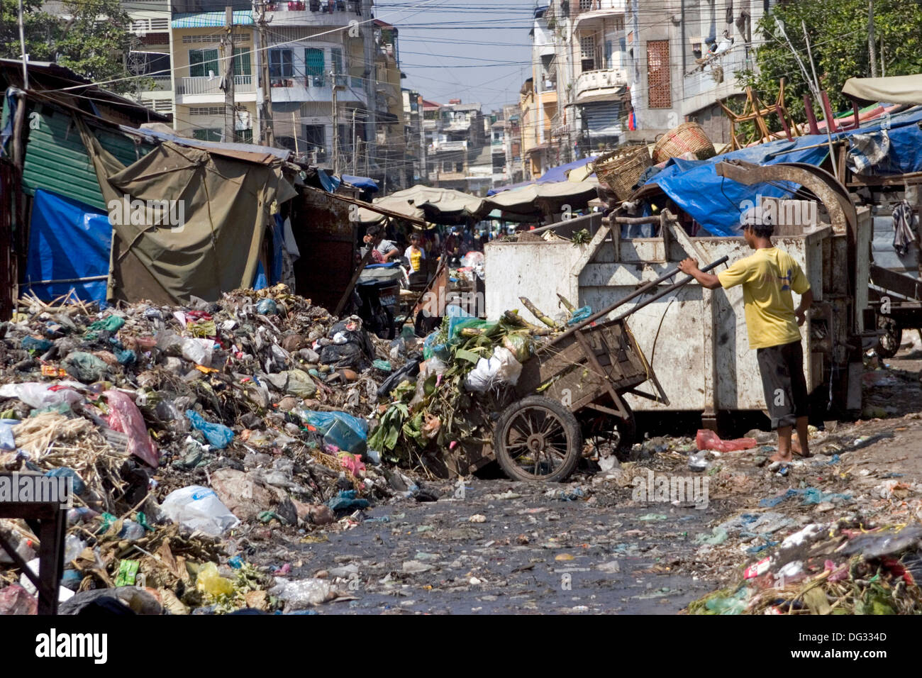 A man is emptying garbage from a wooden cart on a trash strewn street ...