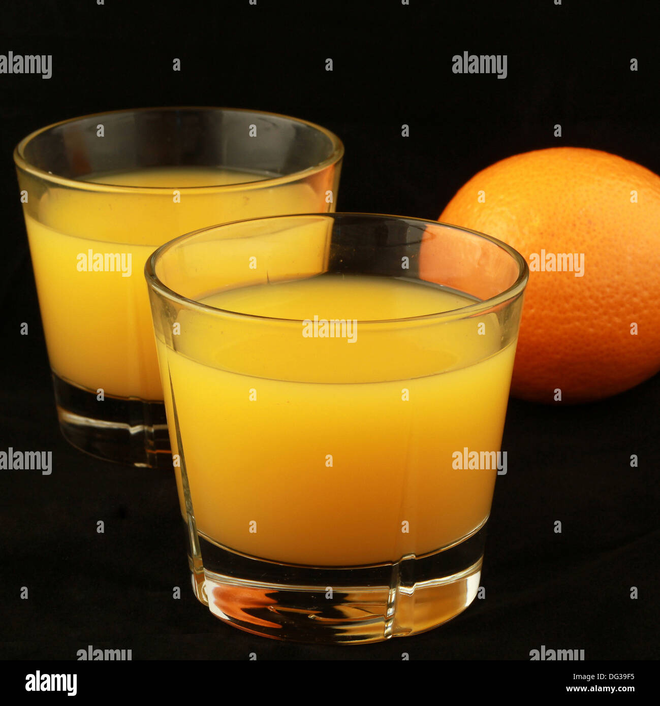 Glasses of orange juice besides orange on black background Stock Photo ...