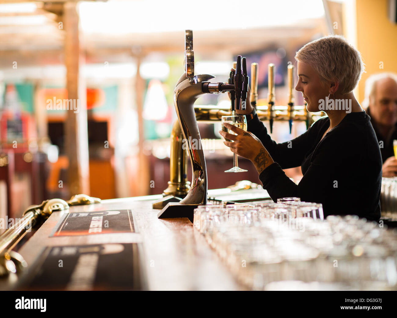 A young woman female bar worker pouring a glass of white wine in a pub ...
