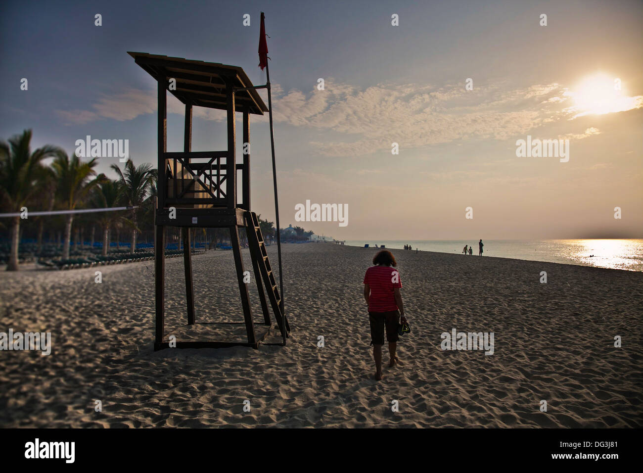 woman walking on beach passing a lifeguard observation deck at sunset ...