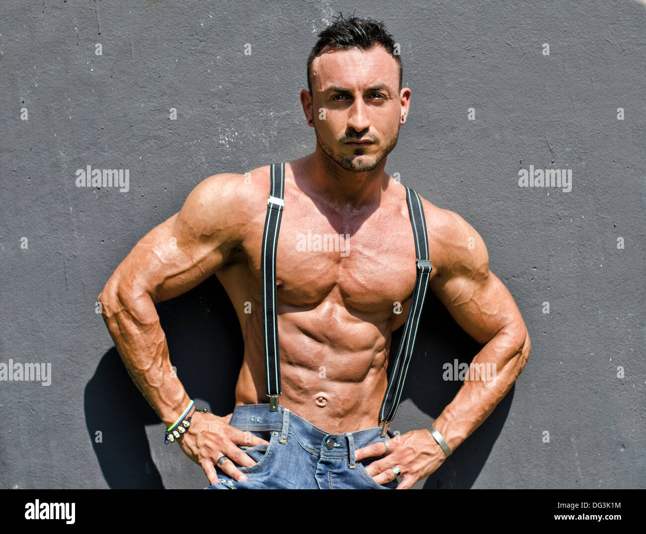 Muscular bodybuilder shirtless with jeans and suspenders against grey ...