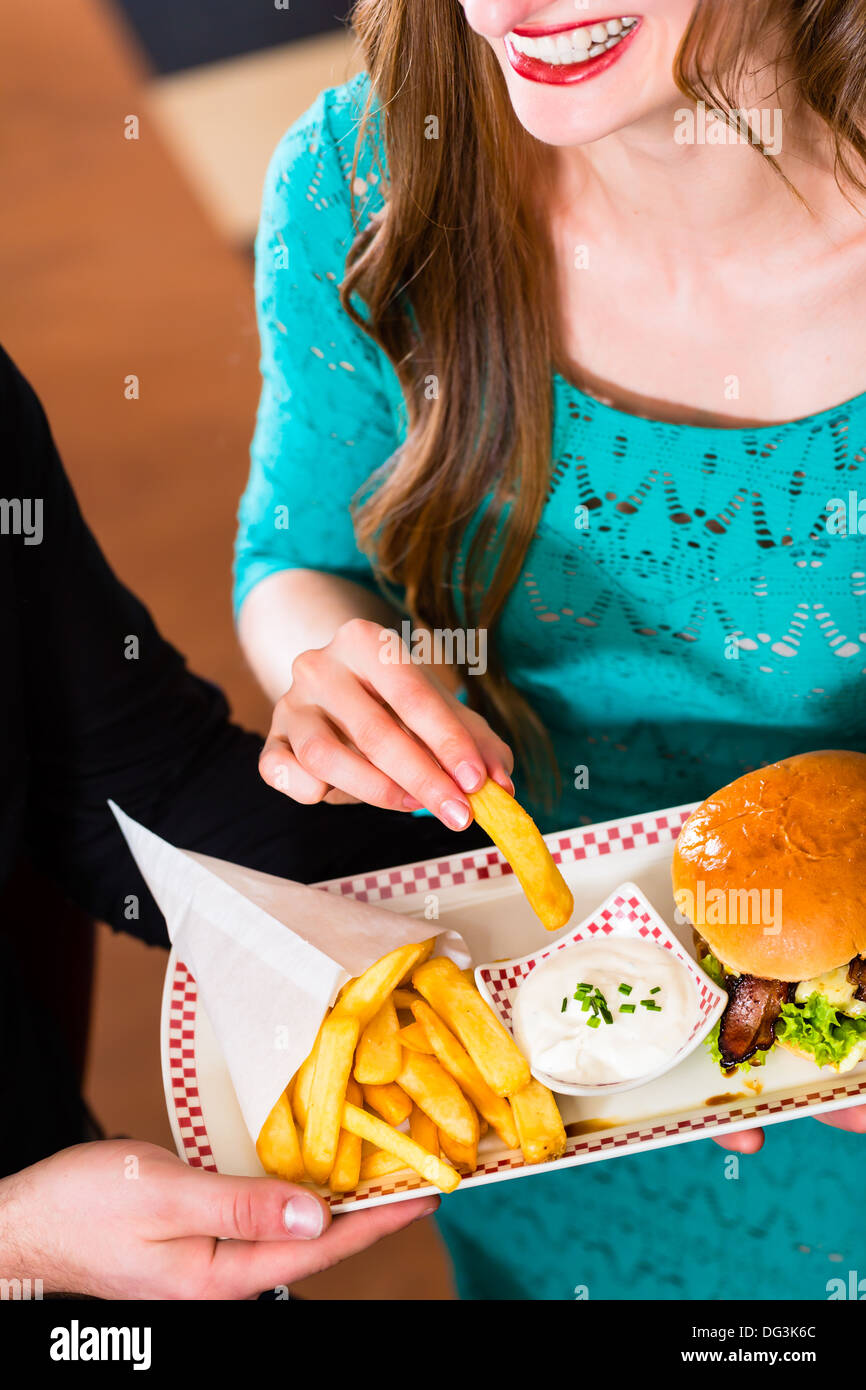 Friends or couple eating fast food with burger and fries in American ...