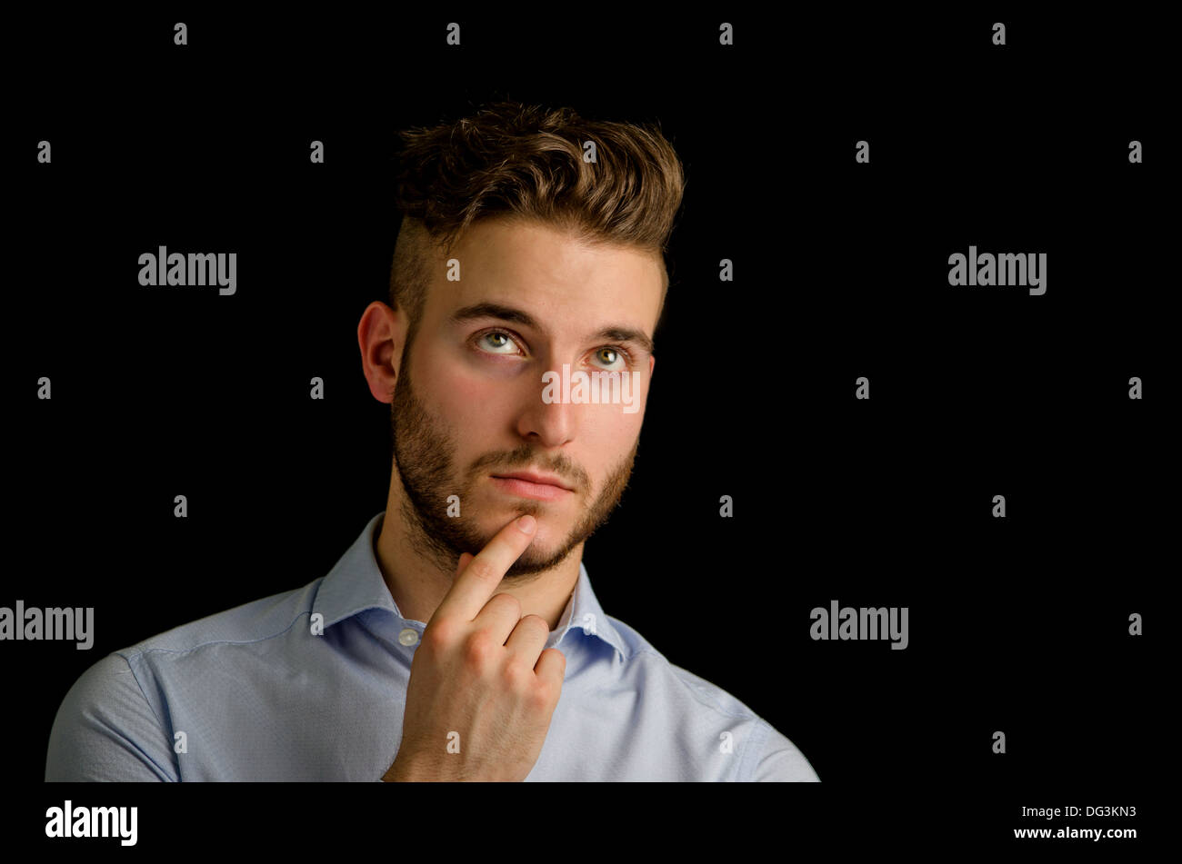 Attractive young man looking up, thinking, isolated on black background ...