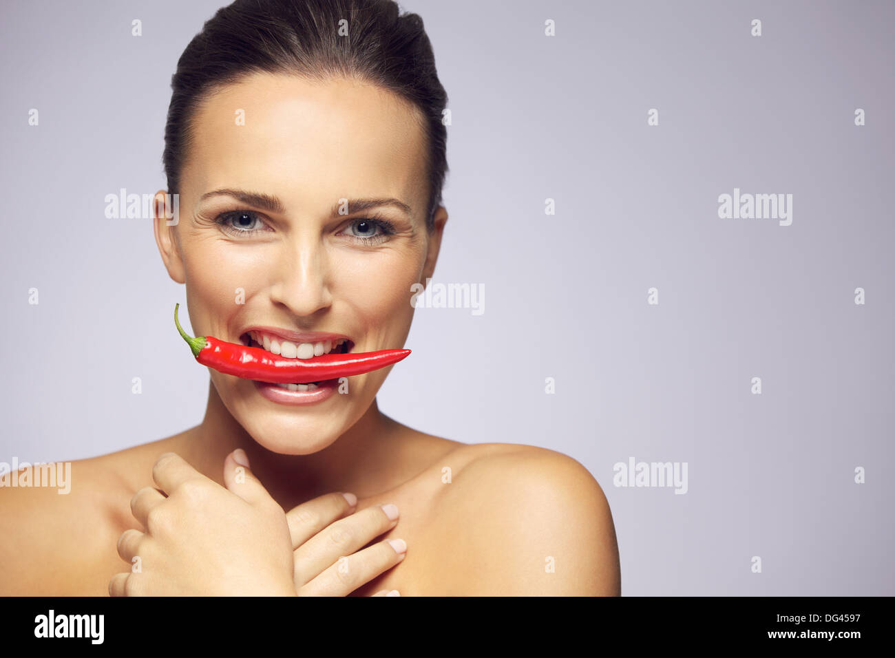 Beautiful young lady having fun, holding red hot chili pepper in mouth ...