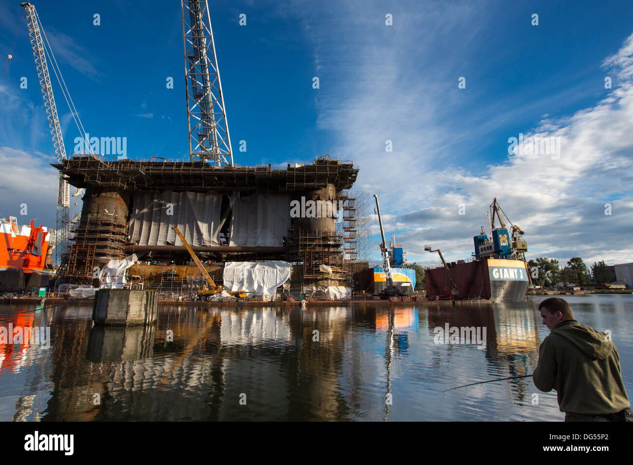 Fisher man fishing in front of a docking oil rig at the Gdansk Shipyard ...