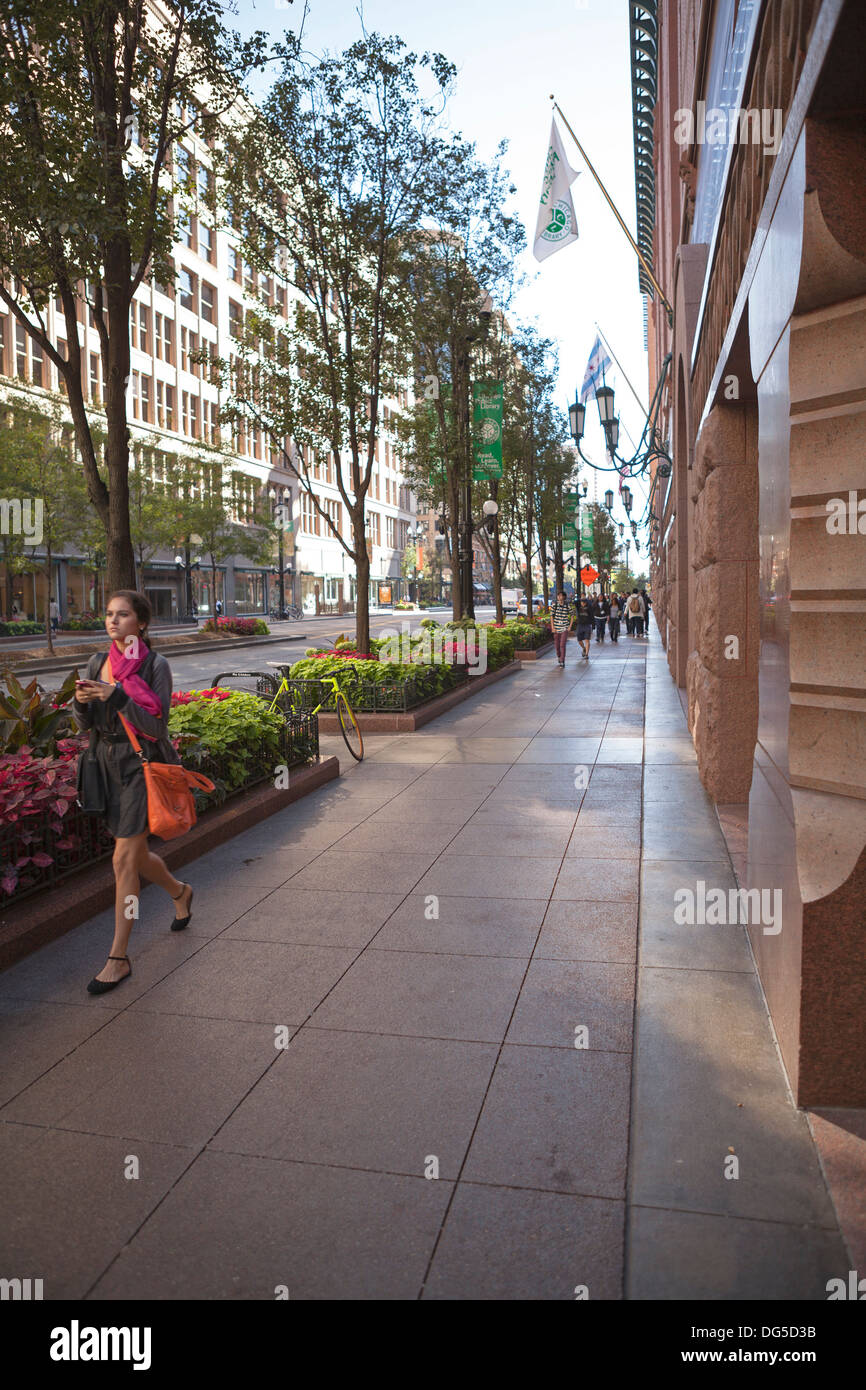 A woman walks on a paved sidewalk with plantings in downtown Chicago ...