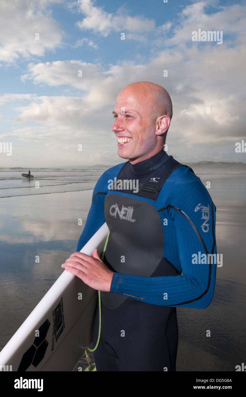 Bald man smiling holding surf board on beach with setting sun Stock ...