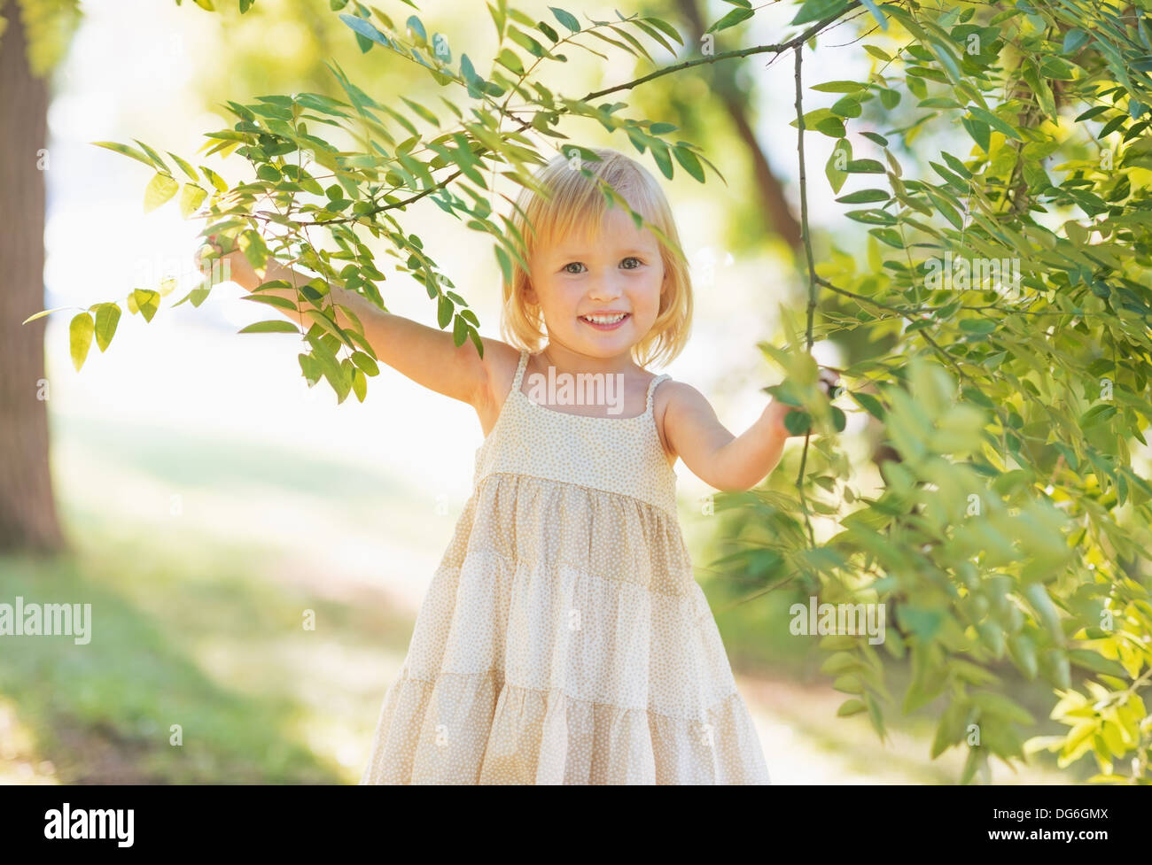 Portrait of smiling baby girl looking out from tree foliage Stock Photo ...