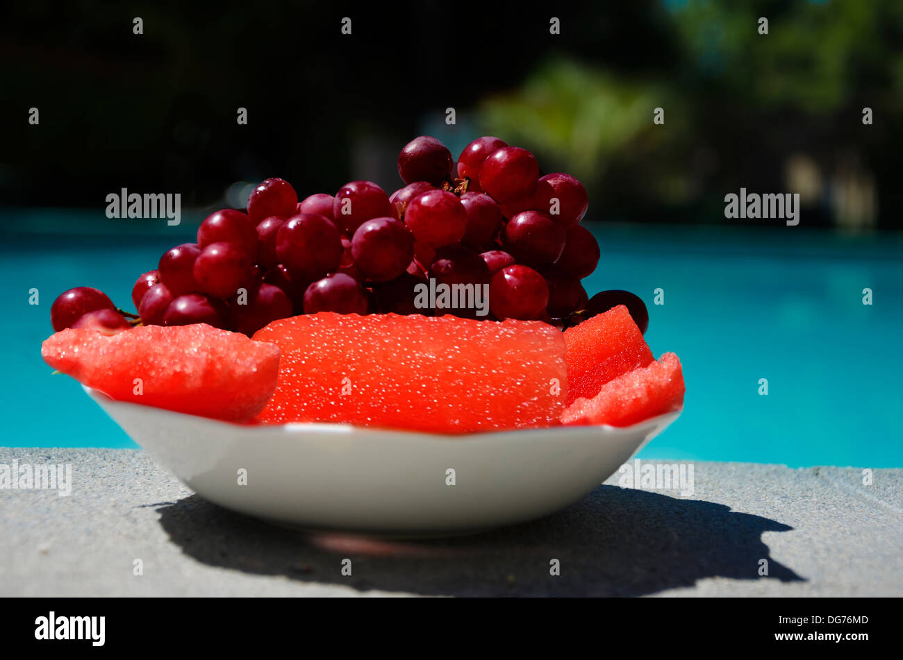 Grapes and watermelon in white plate on table by the swimming pool ...