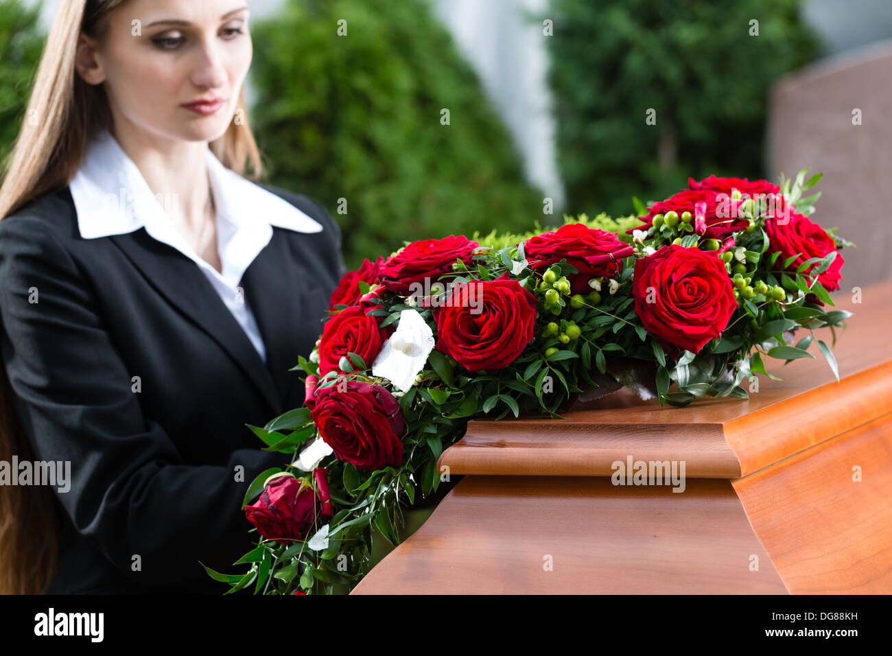 Mourning woman on funeral with red rose standing at casket or coffin ...