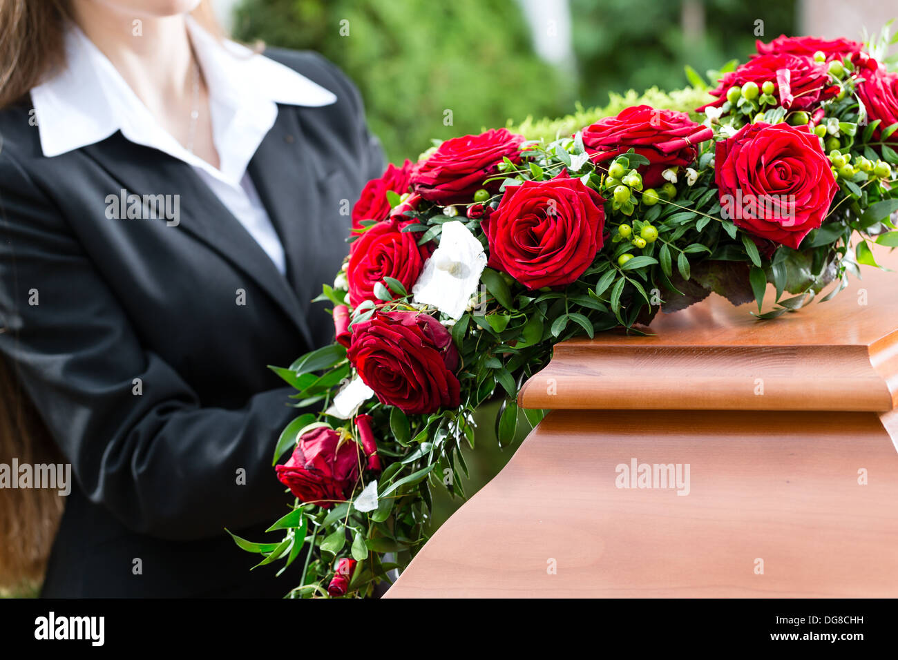 Mourning woman on funeral with red rose standing at casket or coffin ...