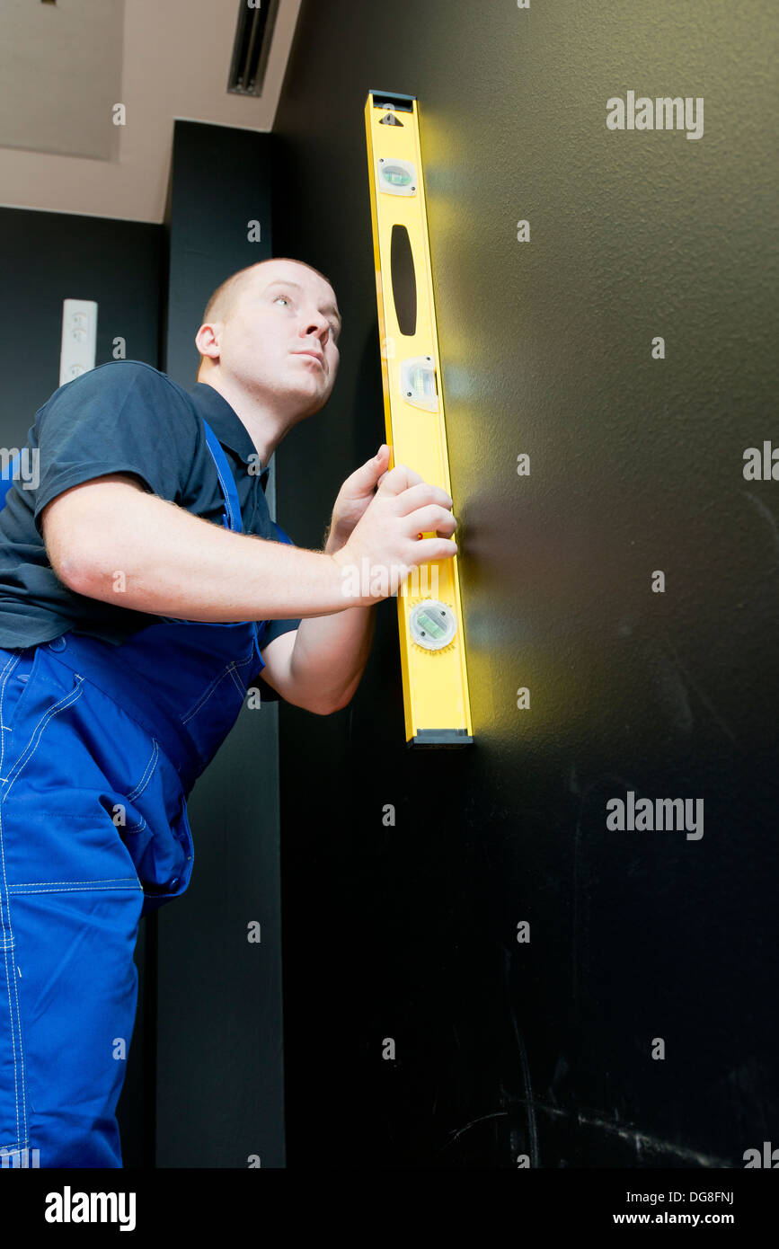 Man using a yellow spirit level on black wall Stock Photo - Alamy