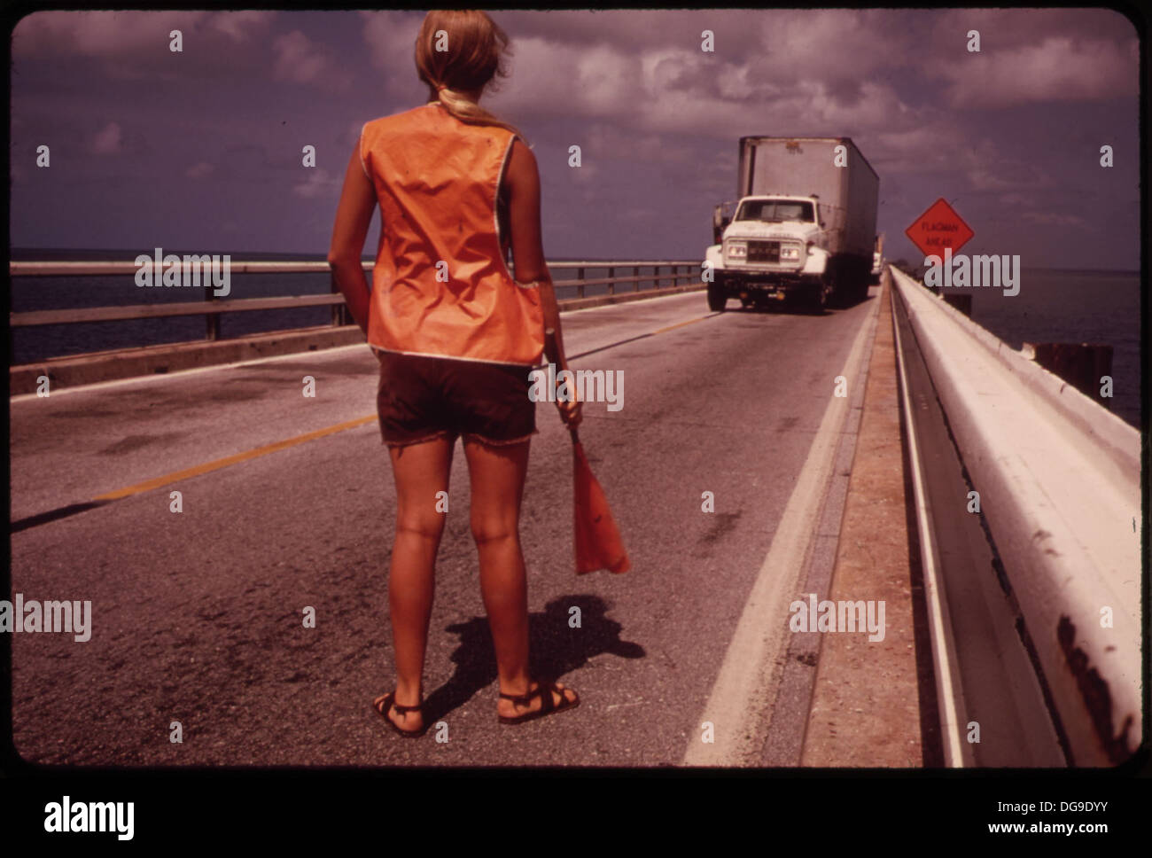 A female road worker directs traffic while repairs are being made to ...