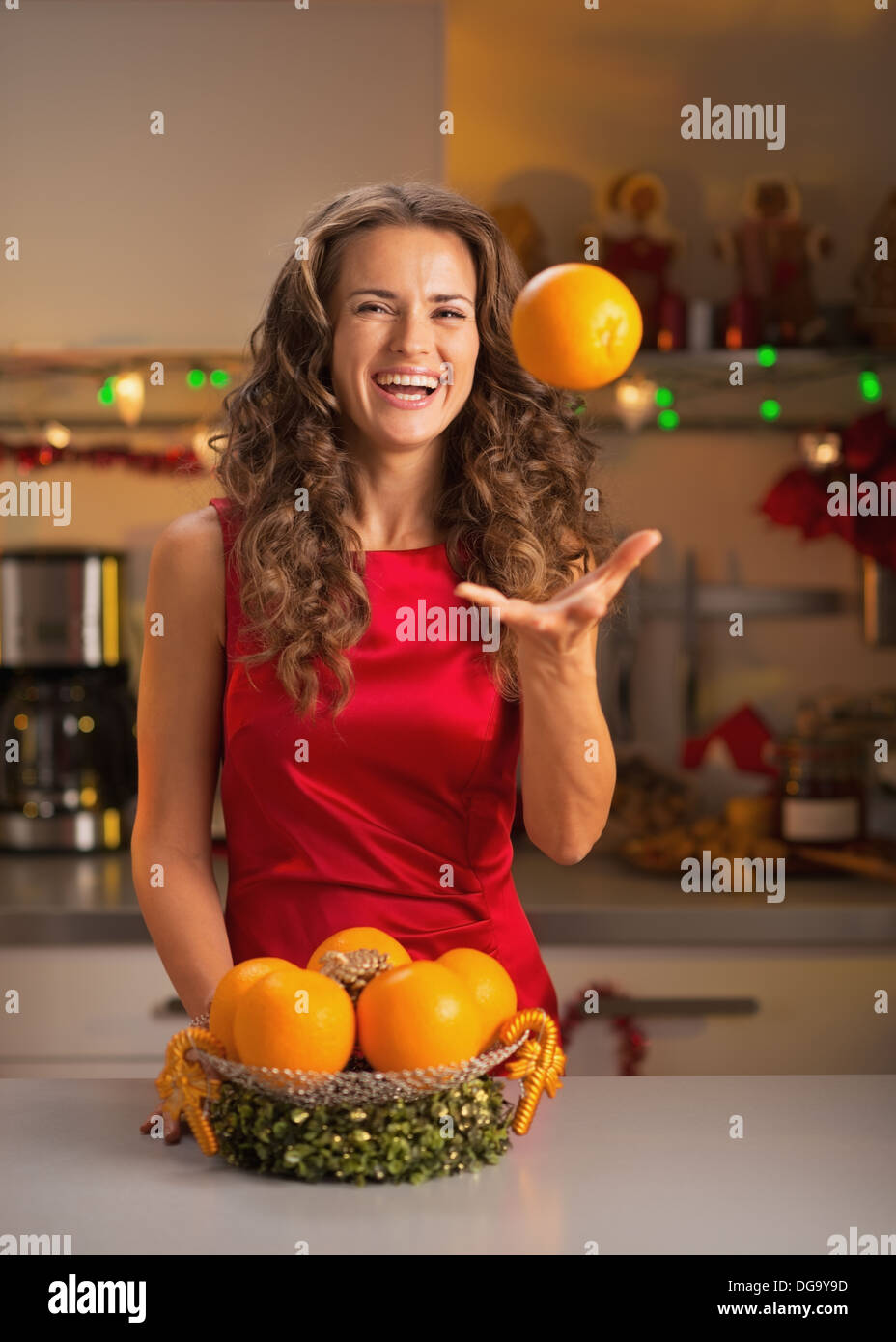 Smiling young woman throwing up orange in christmas decorated kitchen ...