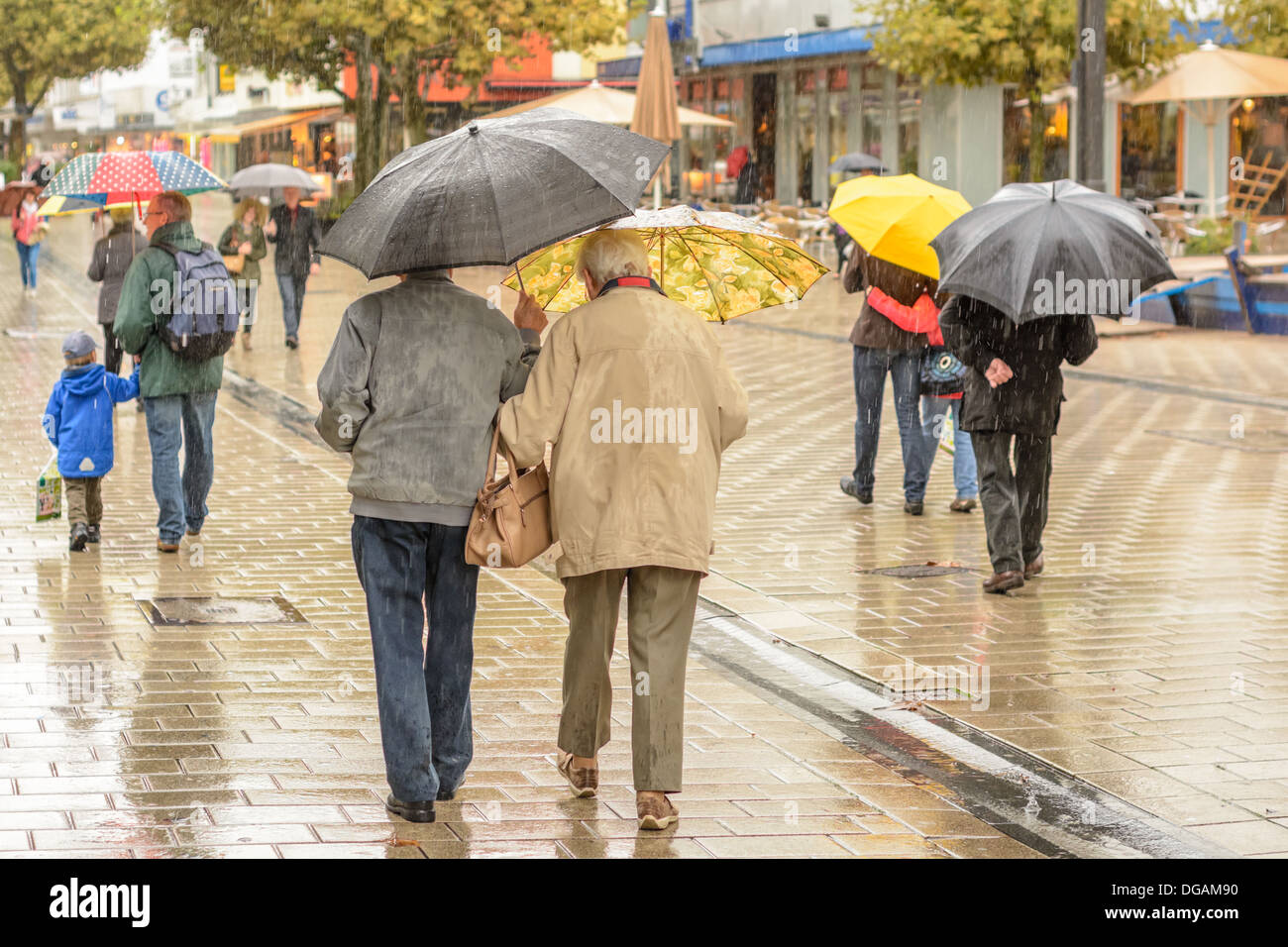 Old senior couple, people with umbrellas, walking trough the rain in a ...