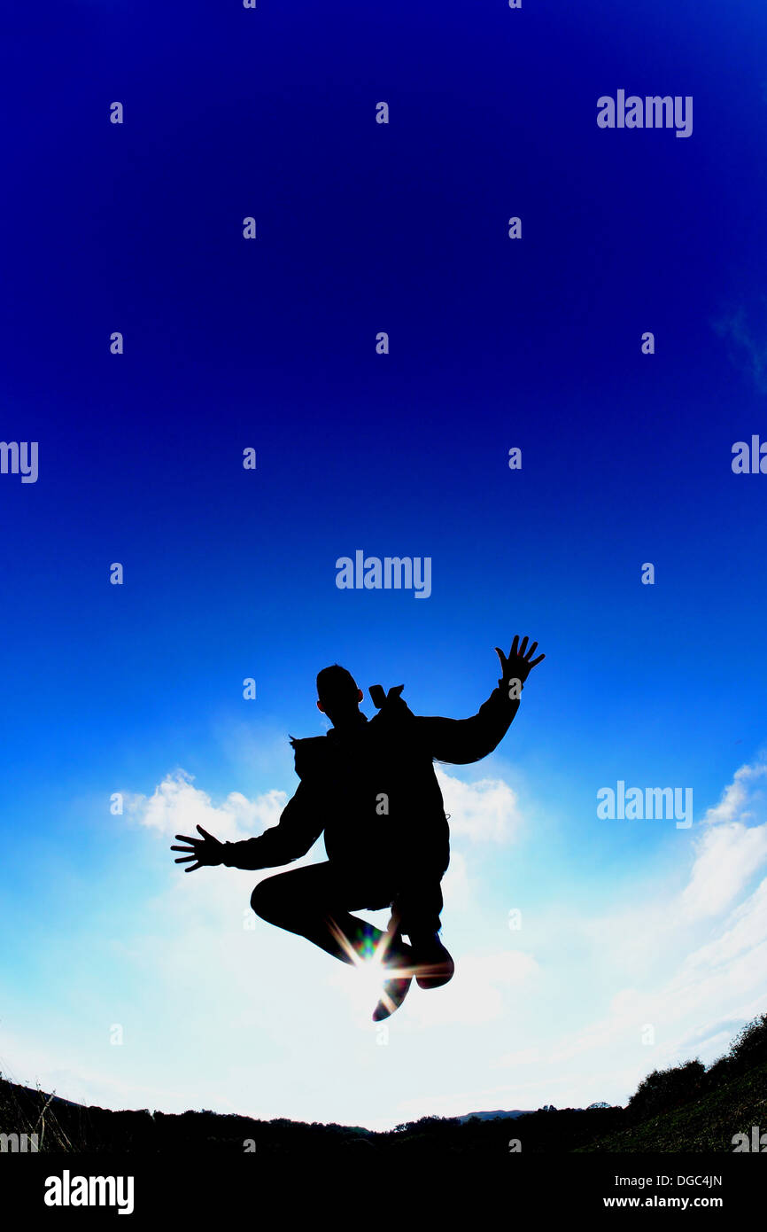 Man jumping against blue sky with sun behind Stock Photo - Alamy