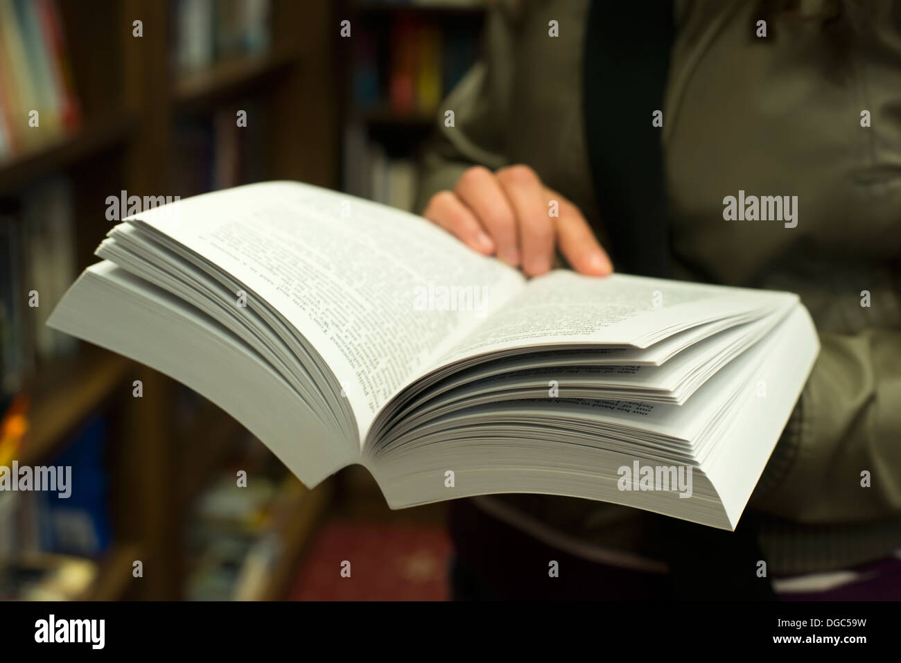 Hand holding open book in a bookstore. Many books on the background ...