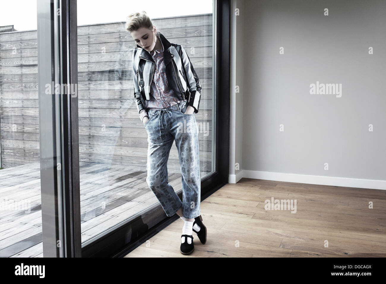 Young woman leaning against window, looking down Stock Photo - Alamy