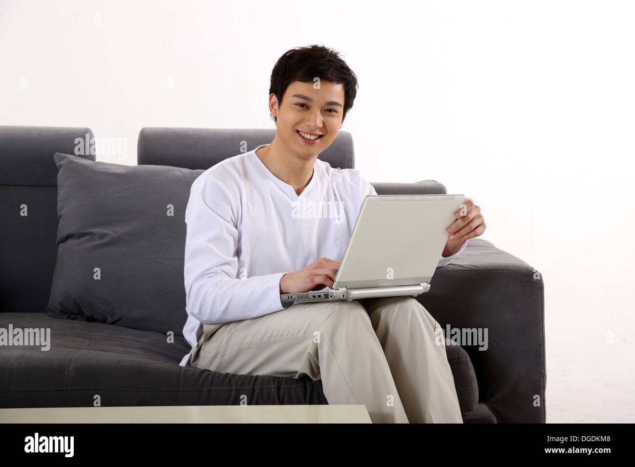 East Asian Man Sitting on the Sofa, Using Computer, Smiling, Looking at ...