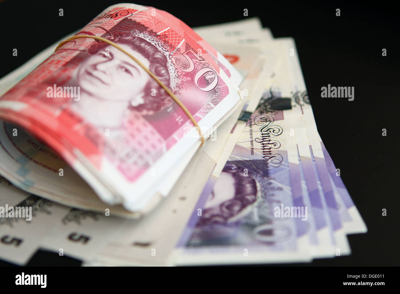 bundles of sterling £50, £20, £10 and £5 notes against a black ...