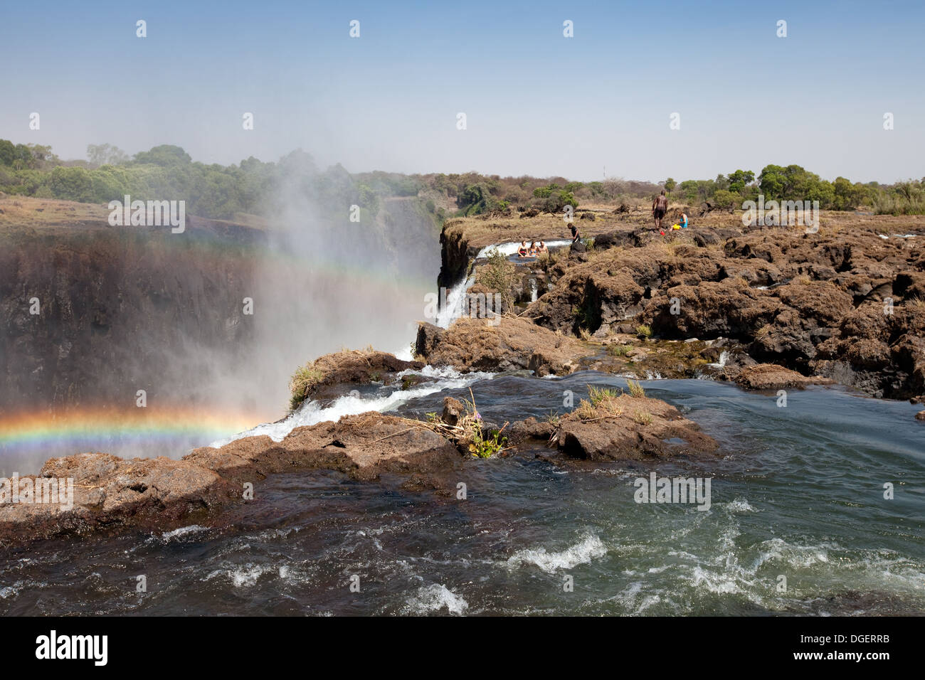 The edge of the Victoria falls with rainbow and people swimming in ...