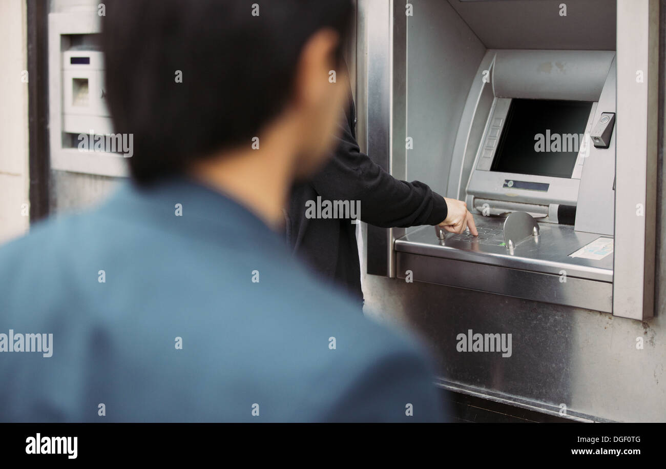 Man withdrawing cash at an ATM with a thief following him Stock Photo ...