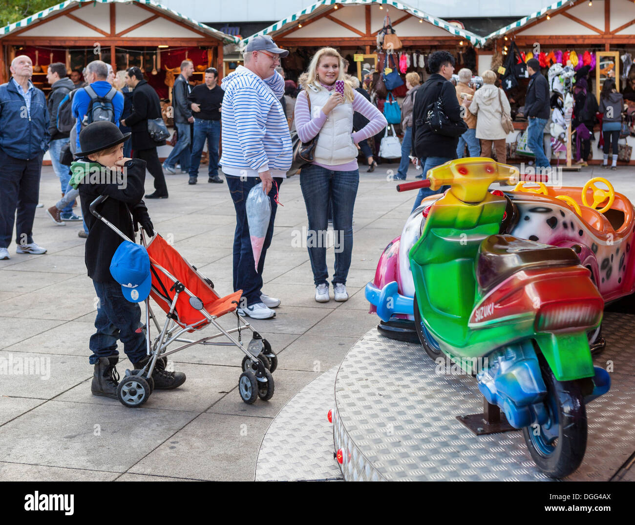 Trendy young boy in bowler hat watching funfair ride at the Oktoberfest ...