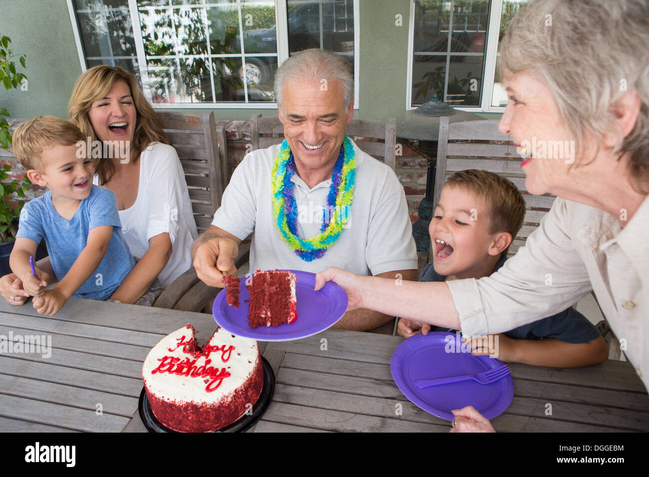 Senior woman serving slice of birthday cake at party with family Stock ...