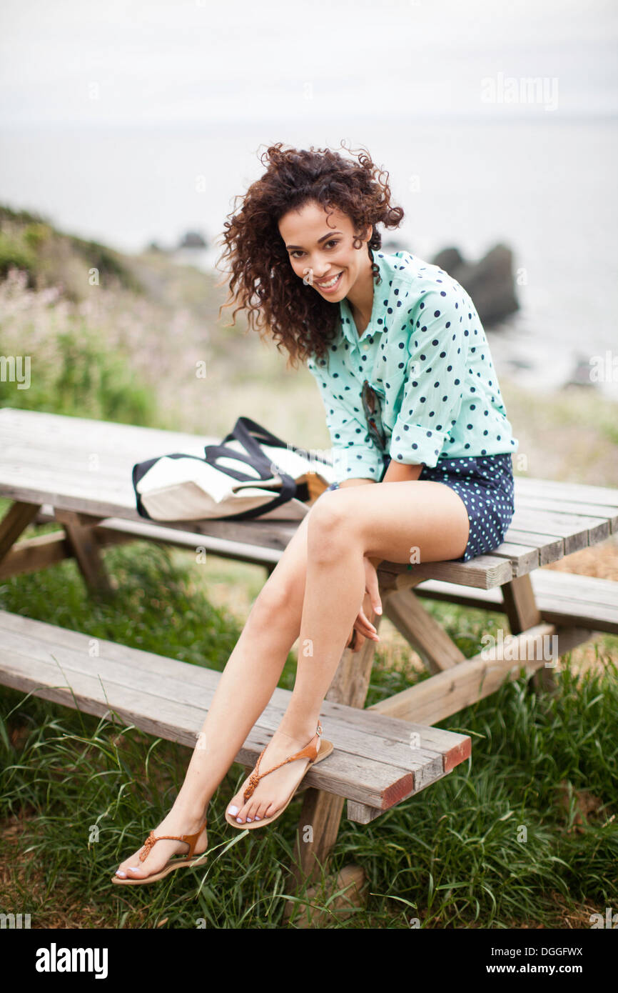 Young woman sitting on picnic table smiling, portrait Stock Photo - Alamy