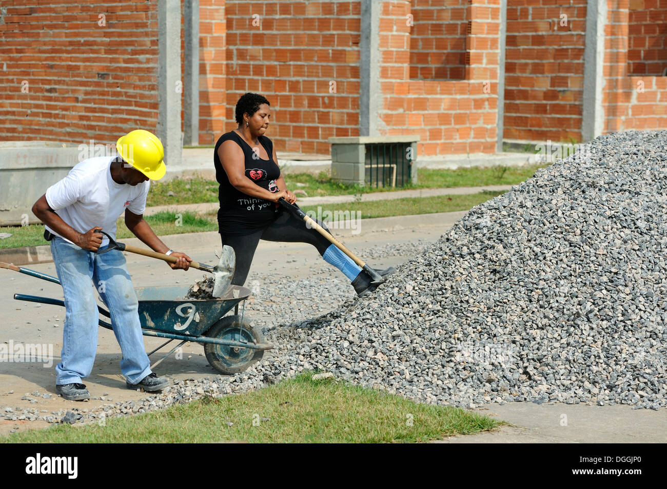 Woman and a man shovelling gravel into a wheelbarrow, they are working ...