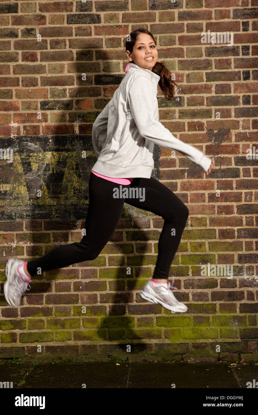 Young woman jumping by brick wall Stock Photo - Alamy