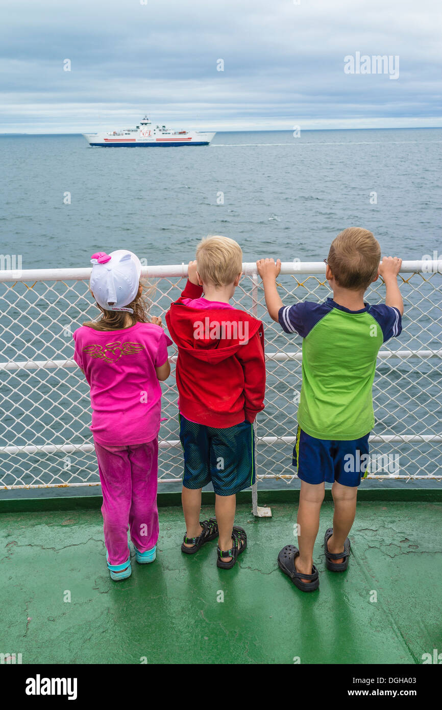 Three kids, 7-10 years of age on a ship, standing at the ship's railing ...