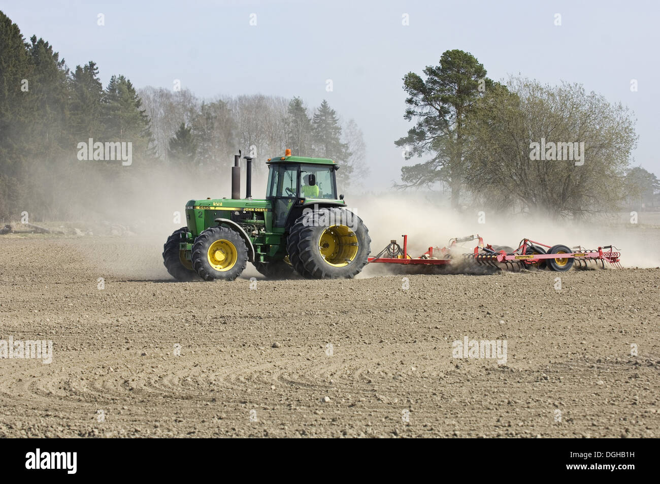 John Deere tractor pulling harrows, harrowing field with wind blown ...