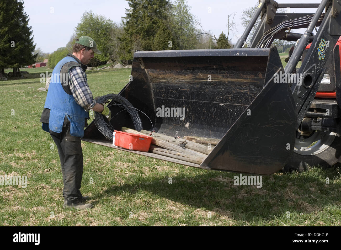 Farmer fencing with barbed wire, collecting coils of wire and posts ...