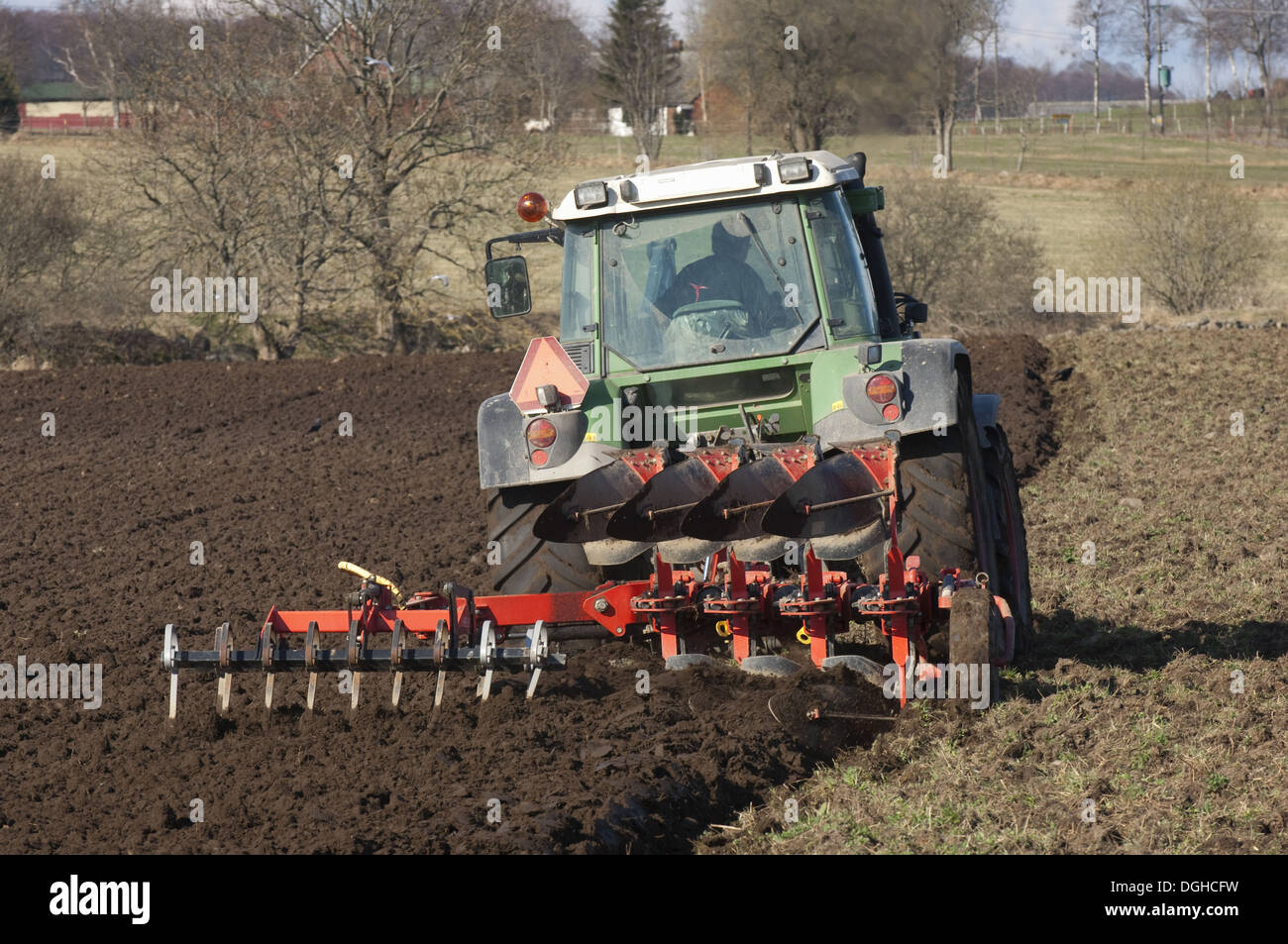 Tractor pulling four furrow reversible plough and small harrow ...