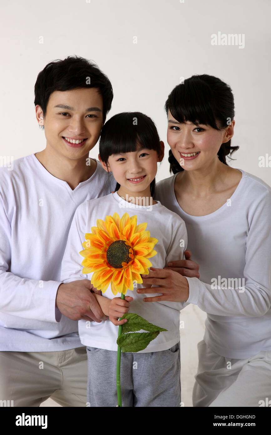 East Asian family with one child embracing, holding sunflower, smiling ...