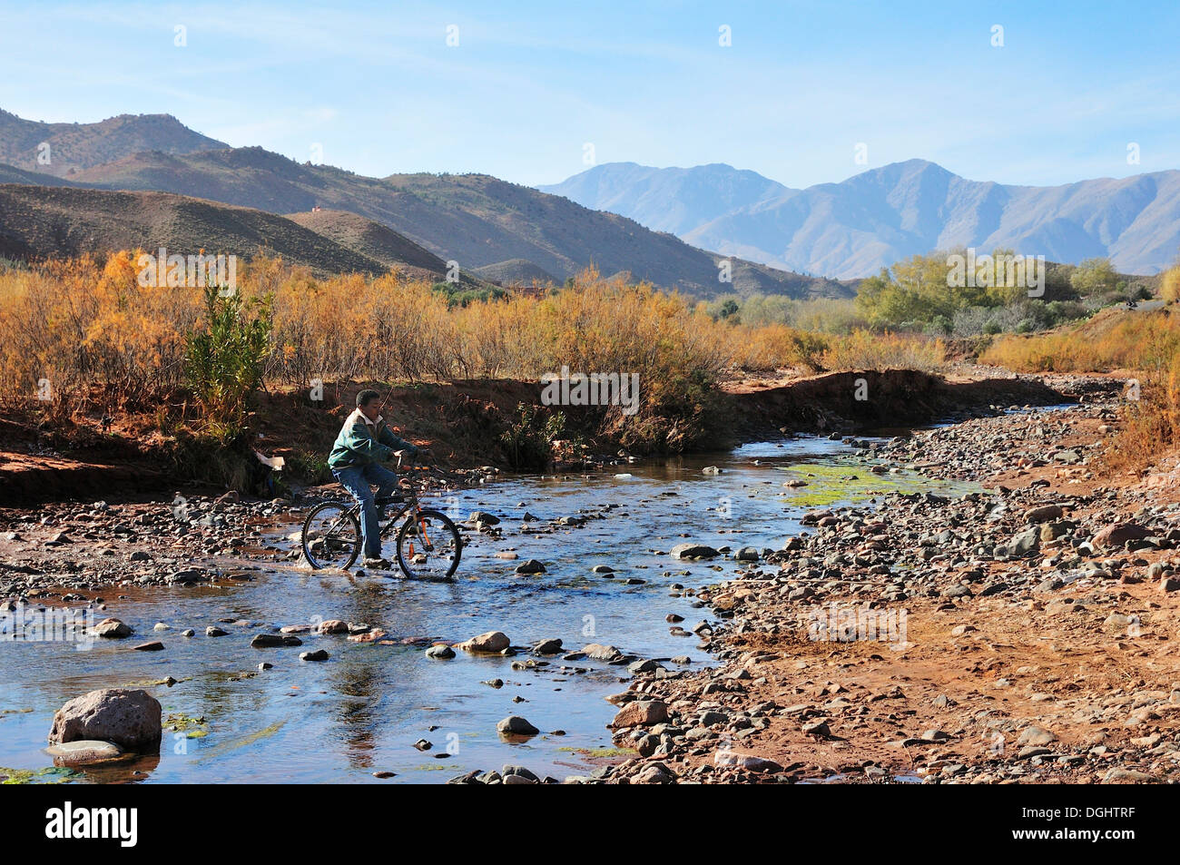 Boy rides his bike through a small river in a barren landscape, Souss ...