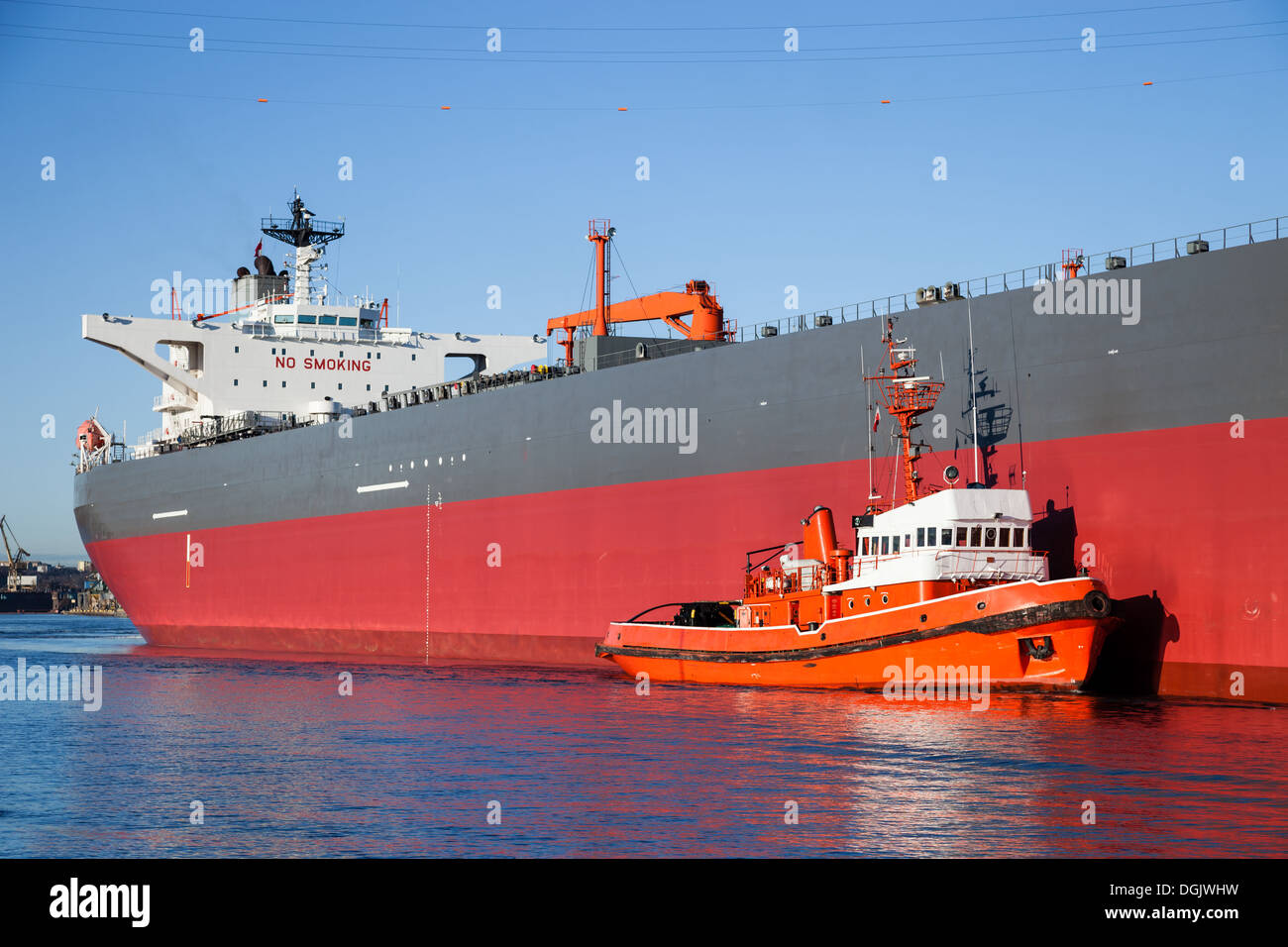 A orange tugboat assisting a large oil tanker Stock Photo - Alamy