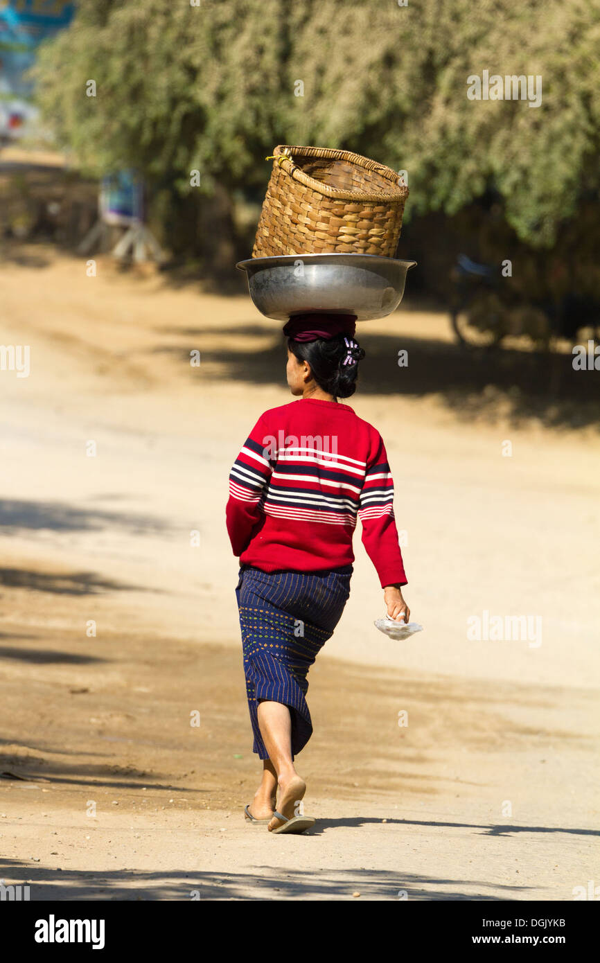 A woman walking whilst balancing a basket on her head in Bagan in ...