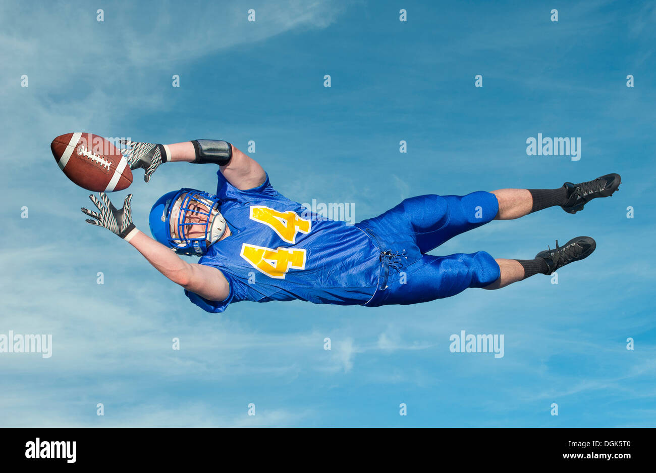 American footballer catching ball against blue sky Stock Photo - Alamy