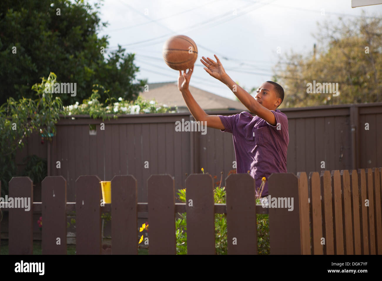 Boy throwing basketball near fence Stock Photo - Alamy